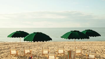 Uma praia com fileiras de espreguiçadeiras e guarda-sóis verdes, dispostas para banho de sol.