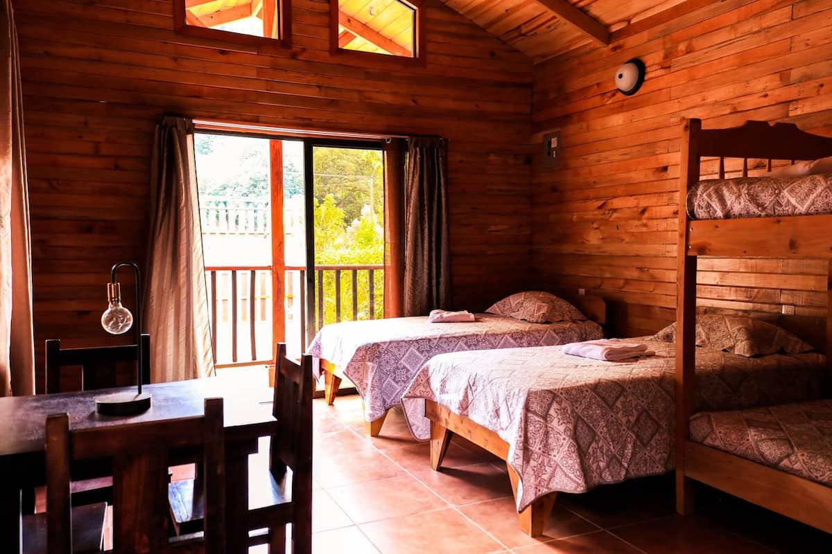 Uma cabana de madeira com duas camas, uma mesa e uma janela com cortinas.