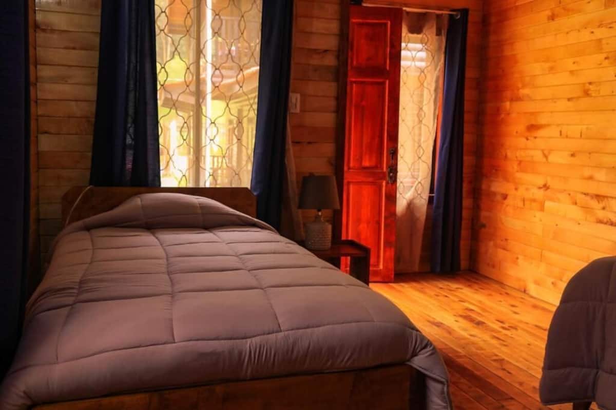 Uma cama de solteiro num quarto com paredes e chão de madeira.
