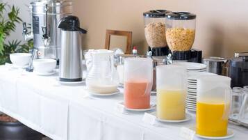 Disposição de buffet com diversos dispensadores de comida e bebida, incluindo uma cafeteira e recipientes para cereais e sumos.