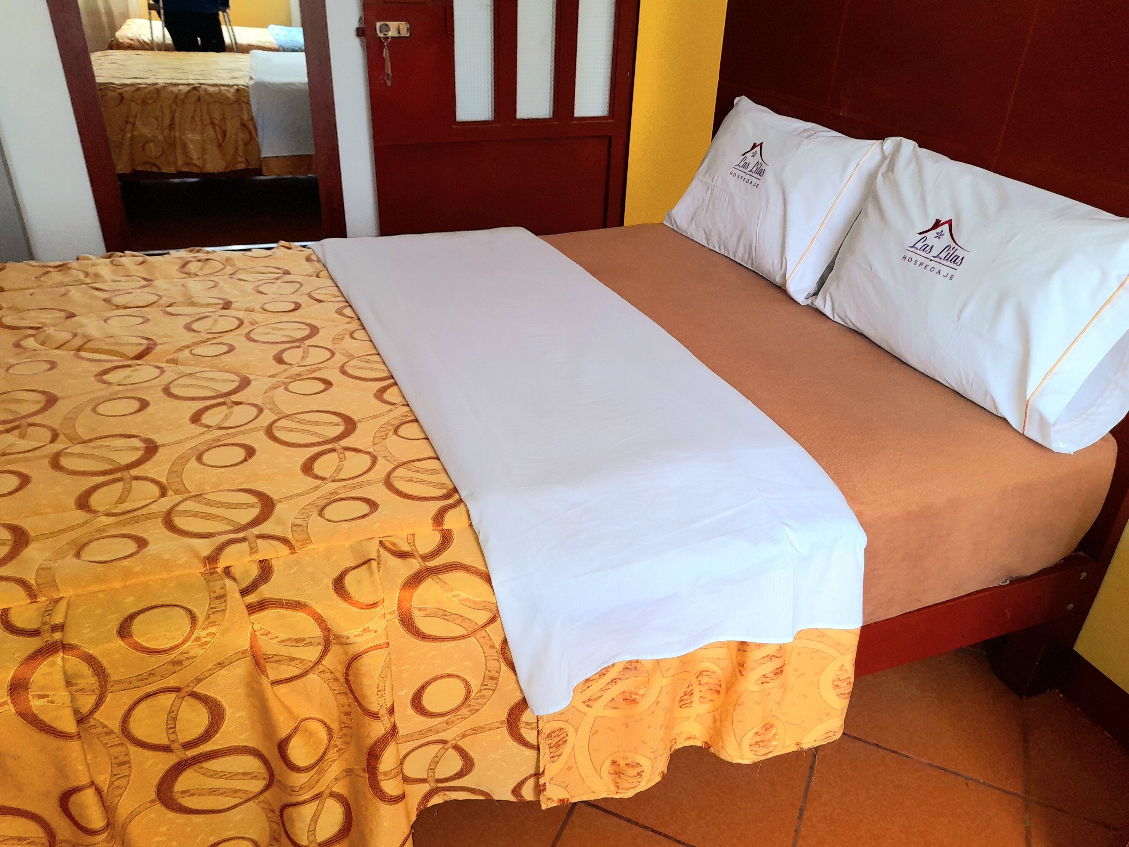 Uma cama com colcha estampada, almofadas brancas e uma porta vermelha ao fundo.