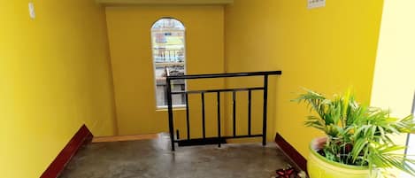 Um corredor amarelo com piso de concreto, corrimão preto e um vaso de planta.