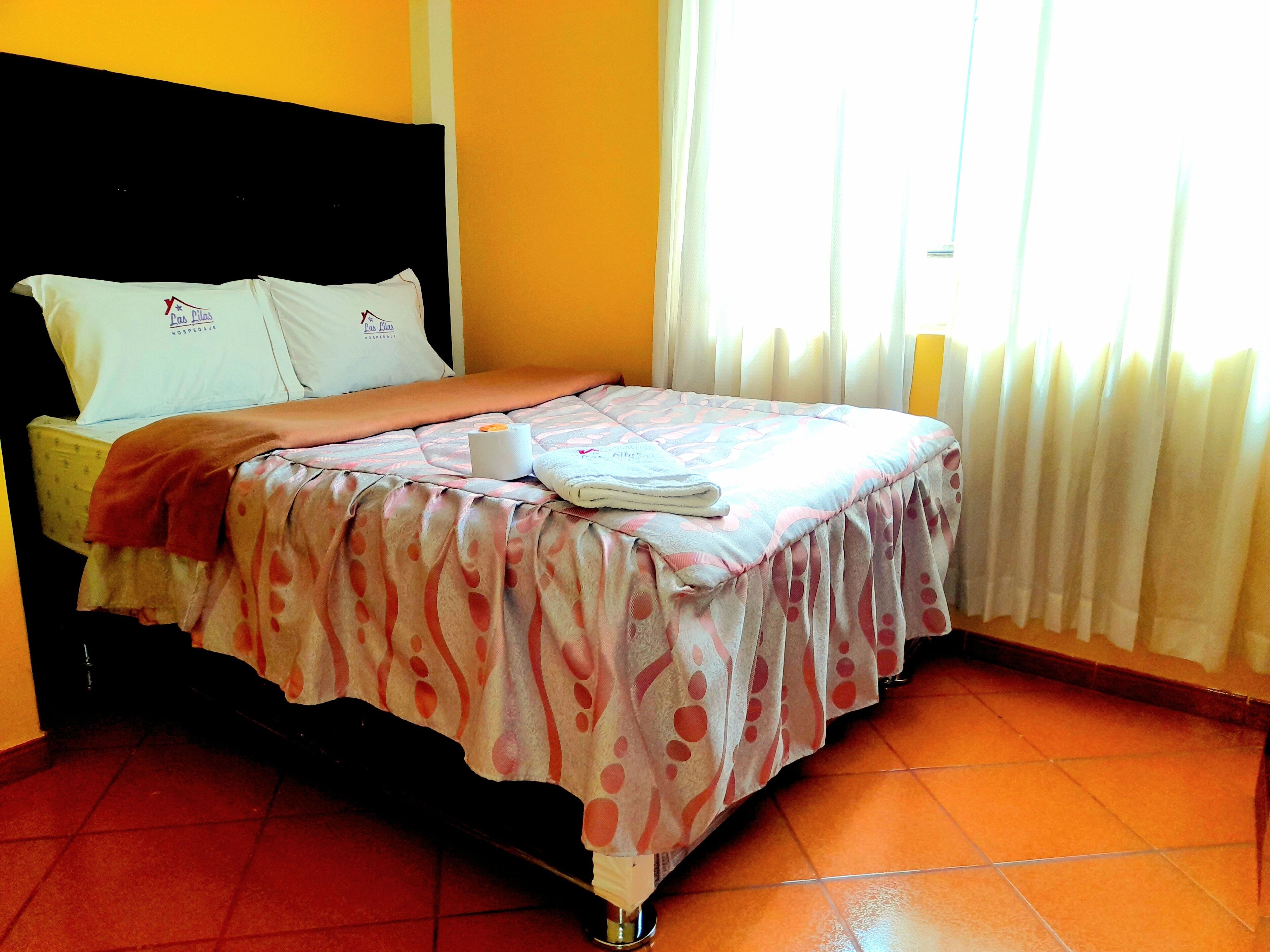Uma cama bem arrumada com um edredom estampado, um travesseiro com um logotipo e uma mesa de cabeceira com uma xícara e uma toalha dobrada.