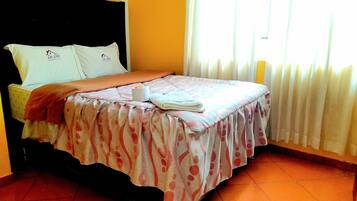 Uma cama bem arrumada com um edredom estampado, um travesseiro com um logotipo e uma mesa de cabeceira com uma xícara e uma toalha dobrada.