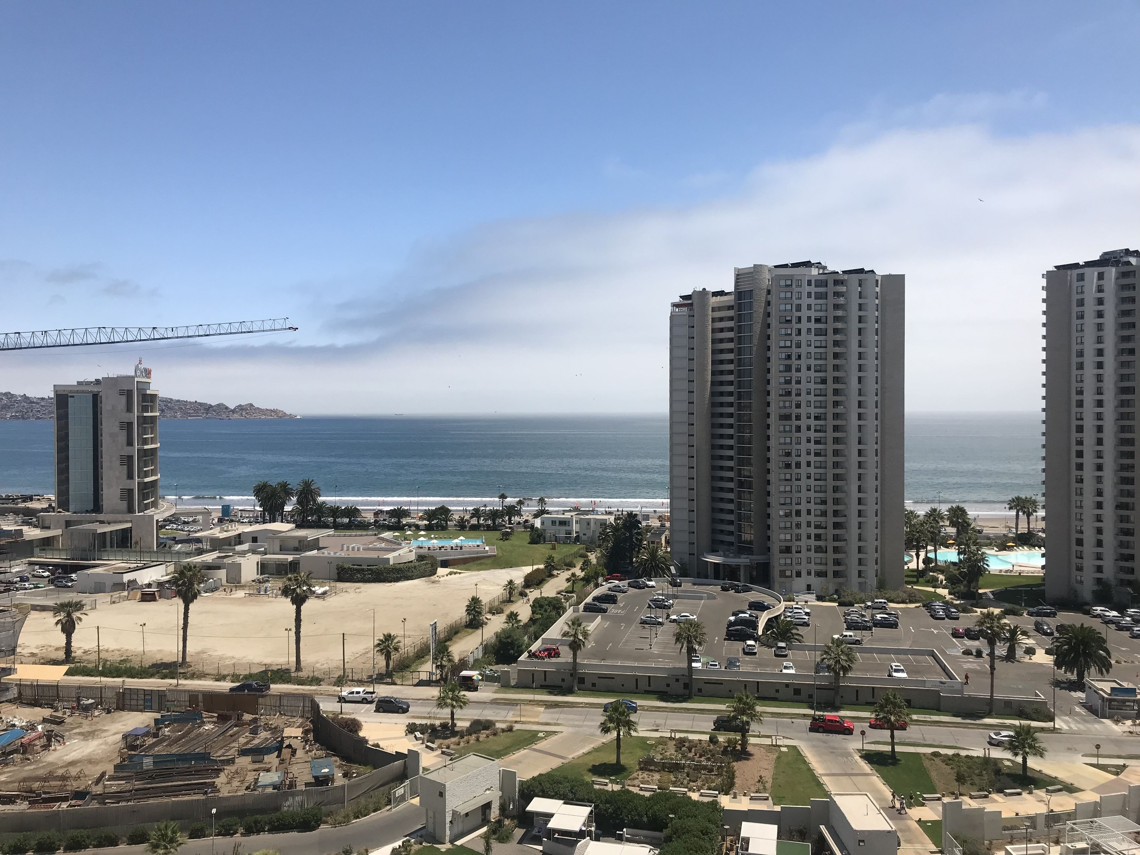 Paisagem costeira urbana com edifícios altos, uma praia e um estacionamento.
