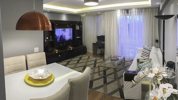 Uma sala de estar moderna com uma televisão de tela plana, uma mesa de centro de vidro e um sofá.