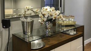 Uma cozinha moderna com bancada de vidro, um vaso de aço inoxidável com orquídeas e uma bandeja com copos.
