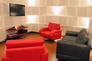 Uma sala de estar moderna com uma televisão de tela plana na parede, um sofá vermelho e um cinza, e um módulo de entretenimento de madeira com aparelhos eletrônicos.