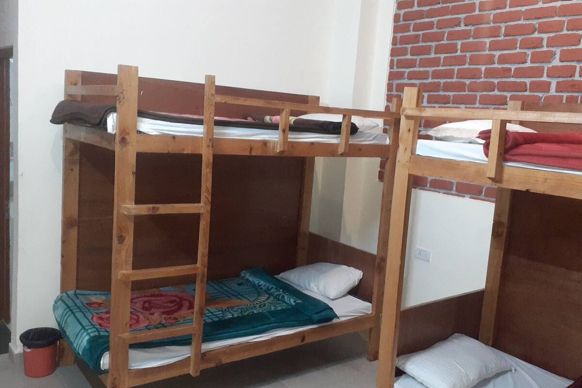 Uma cama beliche com uma escada, uma lixeira vermelha e uma parede de tijolos ao fundo.