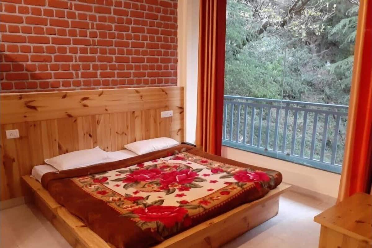 Uma cama de madeira com colcha florida em quarto com parede de tijolos e varanda com guarda-corpo.