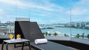 Varanda com vista para a cidade, uma cadeira, uma mesa com copos e uma toalha, e uma janela grande.