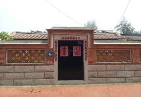 Entrada de um edifício tradicional, com telhado de azulejos, paredes de tijolo e base de pedra.