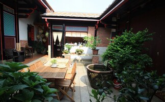 Um pátio japonês tradicional com mesa e cadeiras de madeira, plantas em vasos e uma grande fonte.