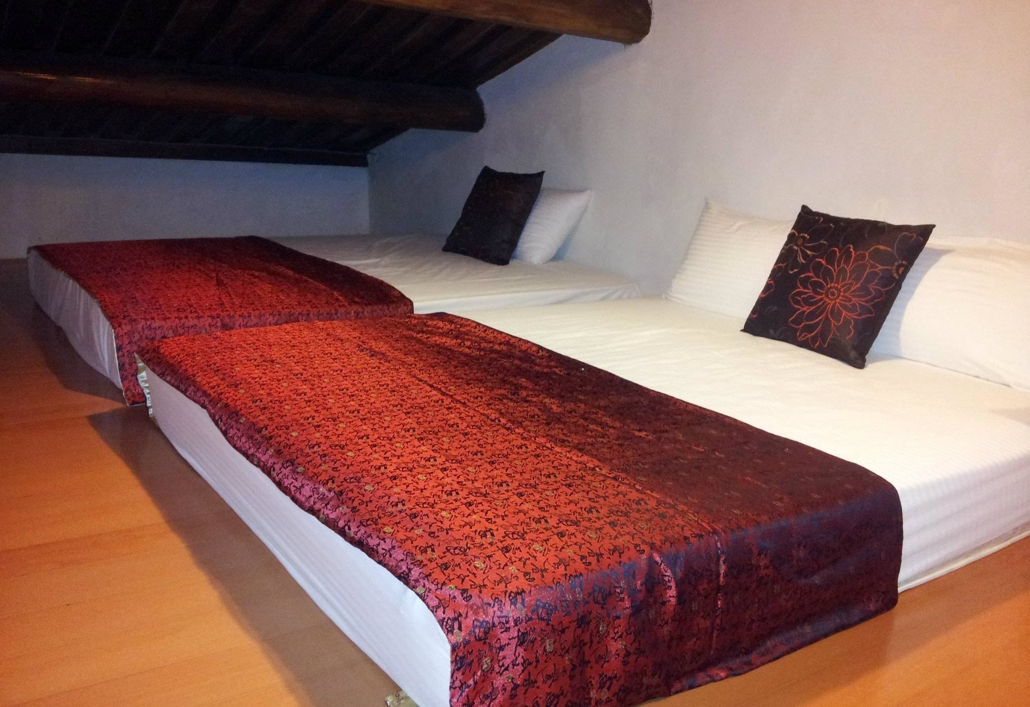 Quarto com duas camas, cada uma com manta vermelha e roupa de cama branca.