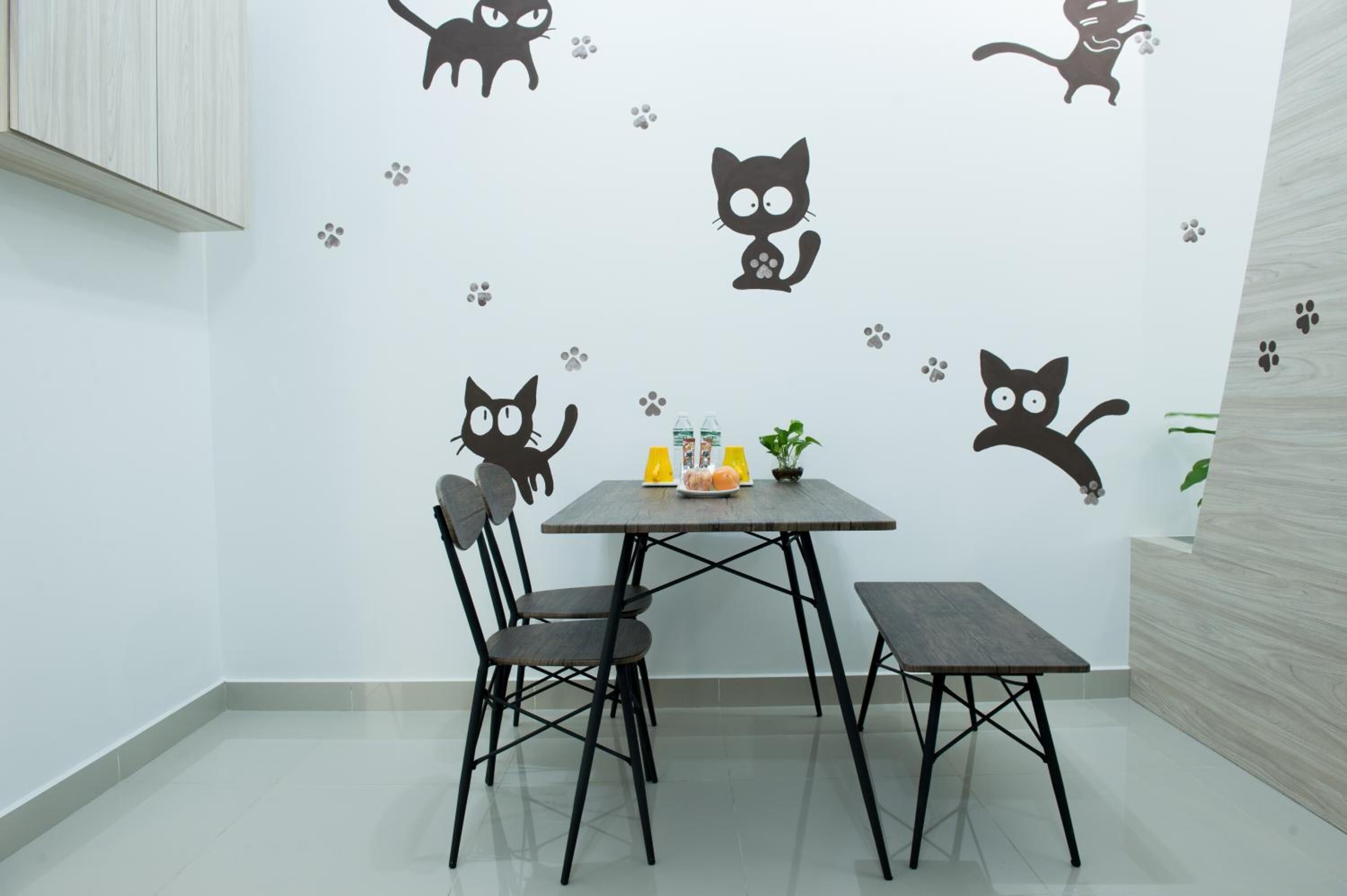 Uma área de refeições com uma mesa, cadeiras e um banco. Há adesivos de parede com gatos e pegadas.