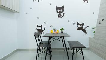 Uma área de refeições com uma mesa, cadeiras e um banco. Há adesivos de parede com gatos e pegadas.