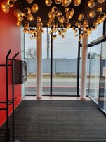 Decoração moderna com entrada de vidro, parede vermelha e luminárias esféricas no teto.