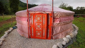 Uma yurt com porta vermelha, rodeada por um caminho de cascalho e uma borda de pedra.