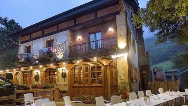 Um edifício rústico com varanda, área de estar ao ar livre e um carro estacionado em frente.