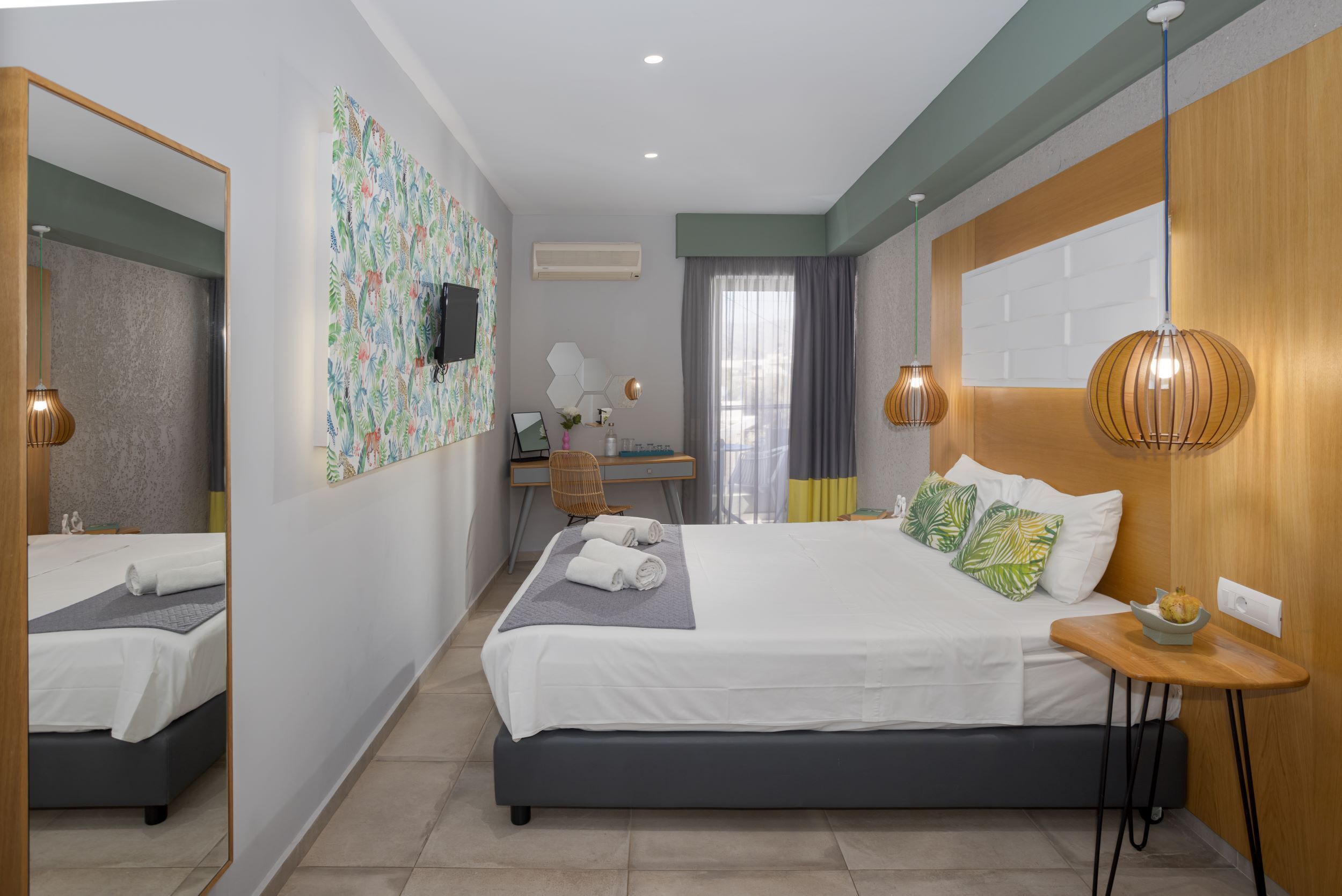 Quarto de hotel moderno com uma cama grande, uma mesa de trabalho, uma cadeira, uma televisão e um espelho.