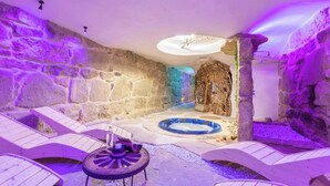 Quarto com paredes de pedra, banheira de hidromassagem, assentos de madeira e uma estrutura decorativa em formato de árvore.