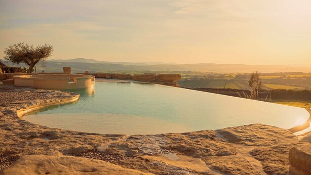 Piscina infinita com vista para colinas distantes e céu claro.