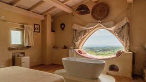 Quarto com uma janela grande, banheira, cama e uma pequena mesa.