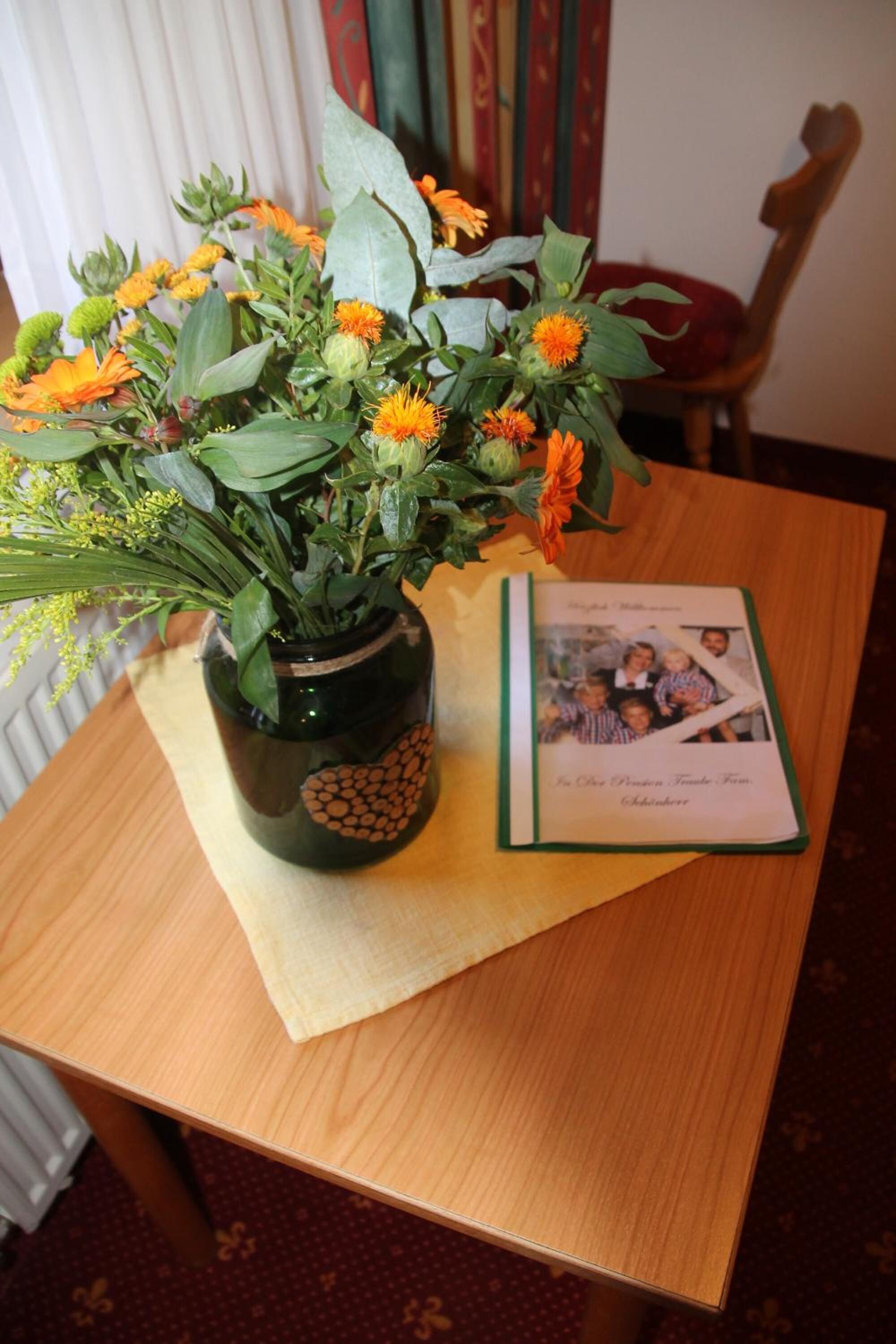 Uma mesa de madeira com um vaso de flores laranjas e uma moldura com foto.