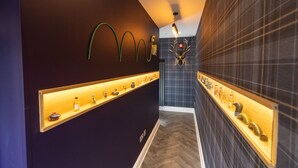 Um corredor com paredes escuras, prateleiras de madeira exibindo garrafas e um ventilador de teto.