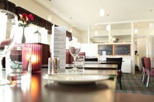 Um ambiente de restaurante com um cardápio, um copo de água e uma vela sobre a mesa.