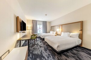Quarto de hotel com duas camas, uma mesa, uma cadeira, uma televisão e uma janela com cortinas.