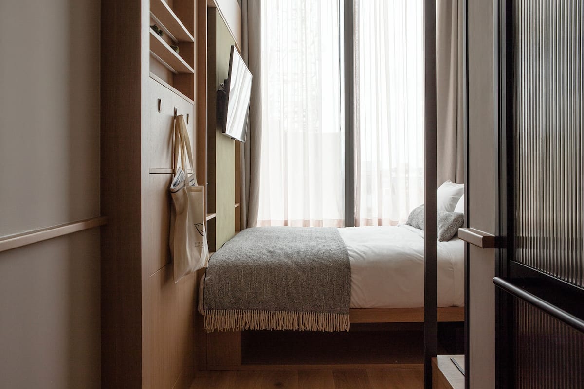 Quarto com cama, guarda-roupa, espelho e janela com cortinas leves.