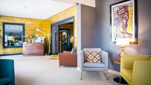 Um lobby moderno com uma mesa de recepção, um sofá com almofada estampada e um quadro na parede.