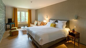 Quarto de hotel com cama grande, sofá, televisão e janela com cortinas.