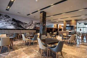 Restaurante moderno com piso de mármore, mobiliário contemporâneo e um mural de montanhas na parede.