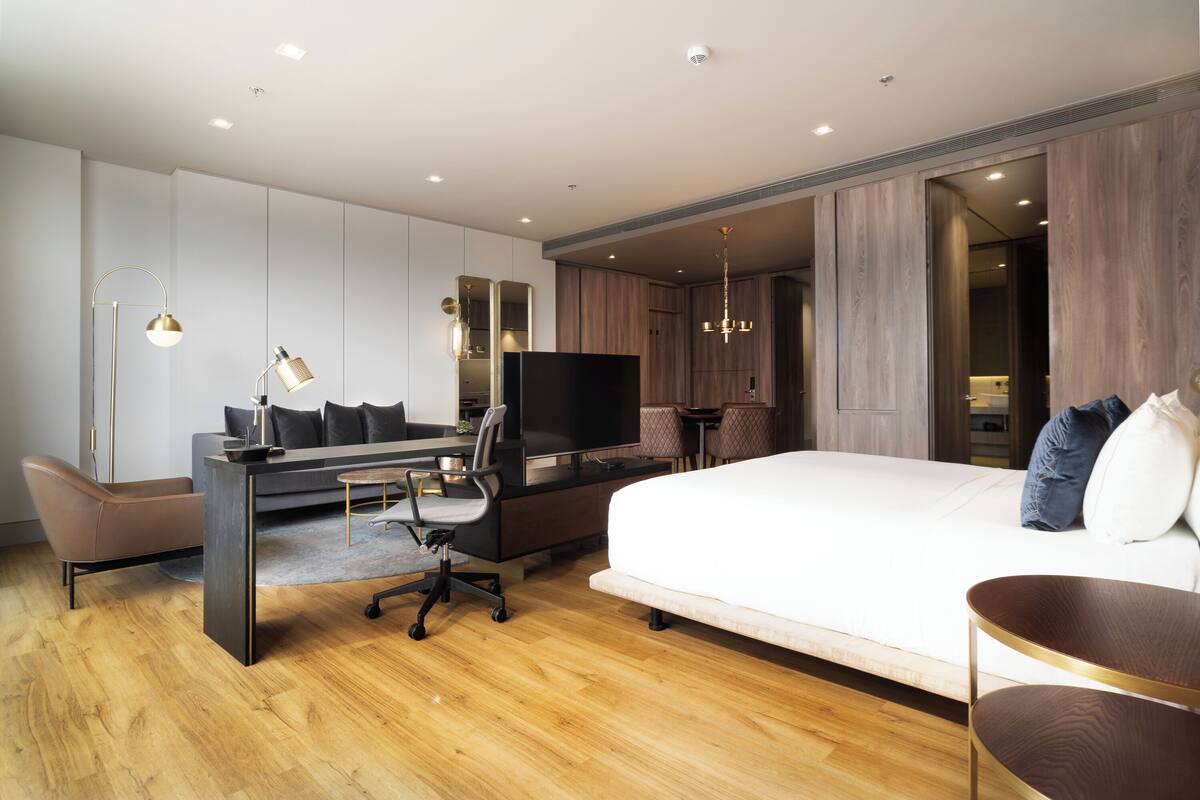 Quarto de hotel moderno com uma cama grande, uma escrivaninha com televisão de tela plana, um sofá e um espaço de refeições.