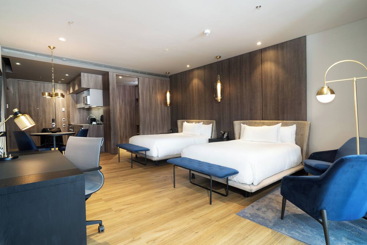 Quarto de hotel moderno com duas camas, uma escrivaninha e uma cadeira.
