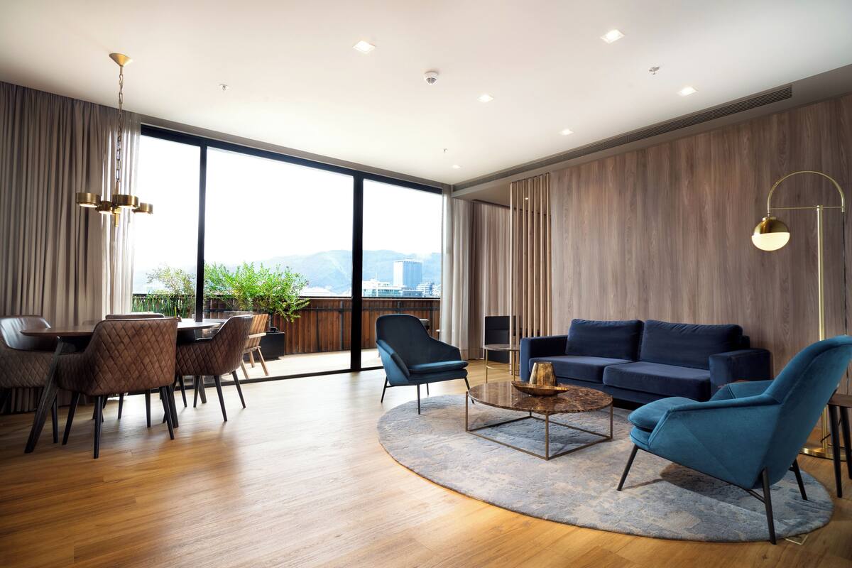 Uma sala de estar ampla, com mesa de jantar, sofás e uma janela grande com vista para a cidade.