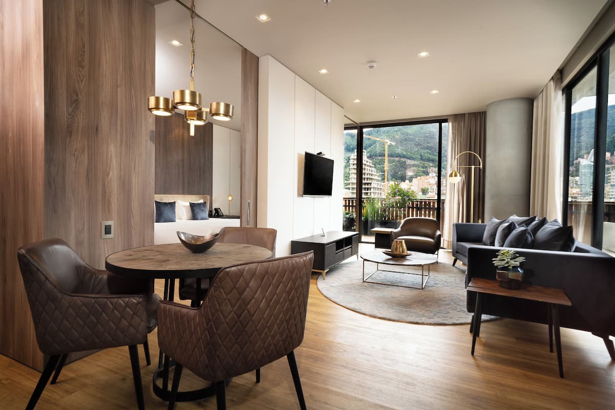Uma sala de estar moderna com uma mesa de jantar redonda, cadeiras de couro, um sofá e uma grande janela com vista para a cidade.