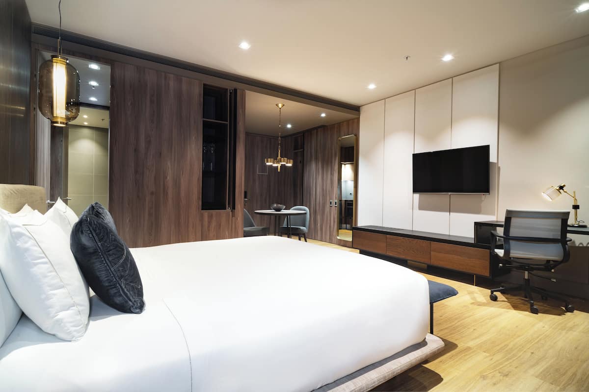 Quarto moderno com cama grande, escrivaninha, cadeira e TV na parede.