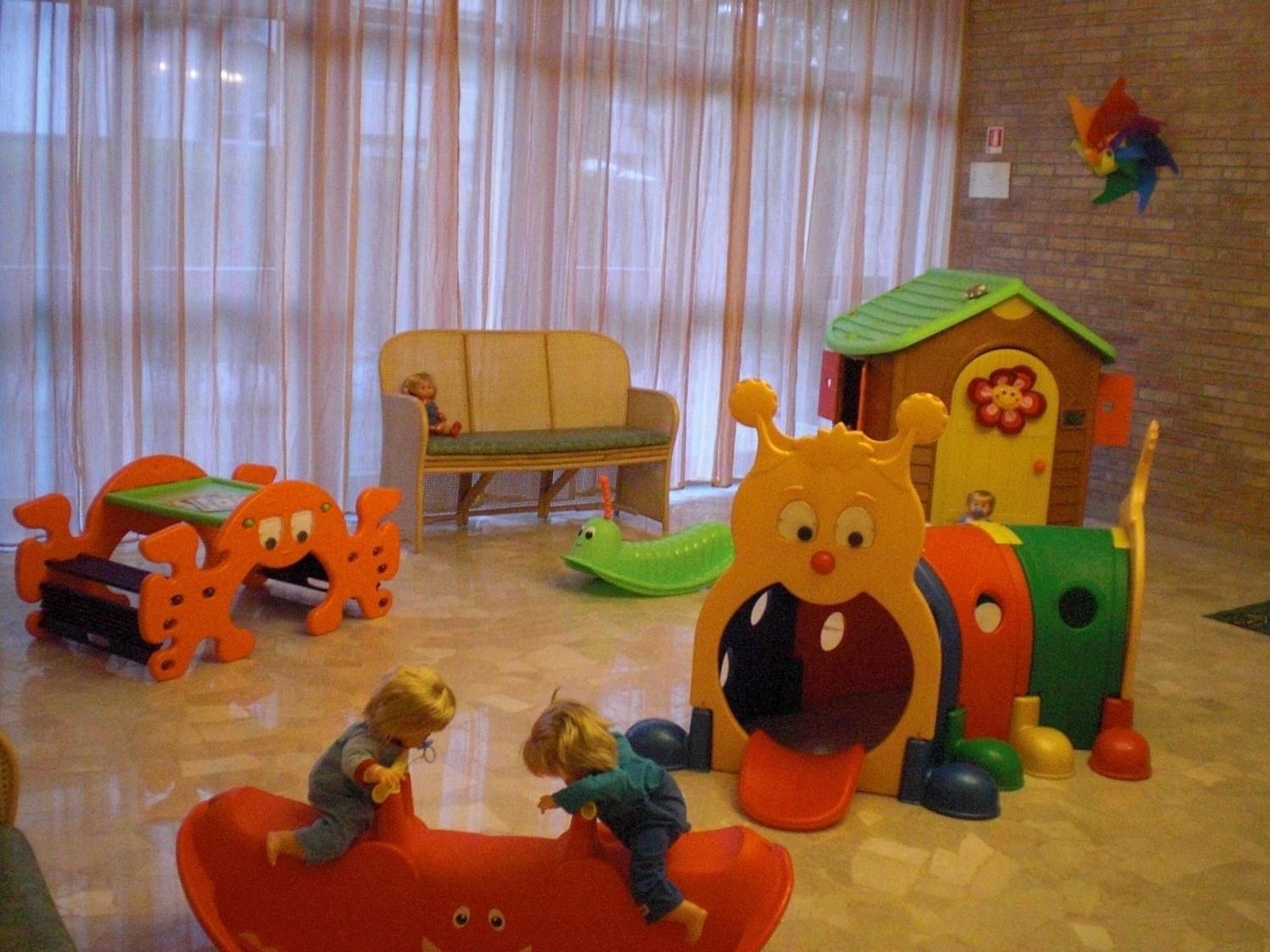 Uma área de recreação infantil com estruturas coloridas, um banco e um girassol decorativo na parede.