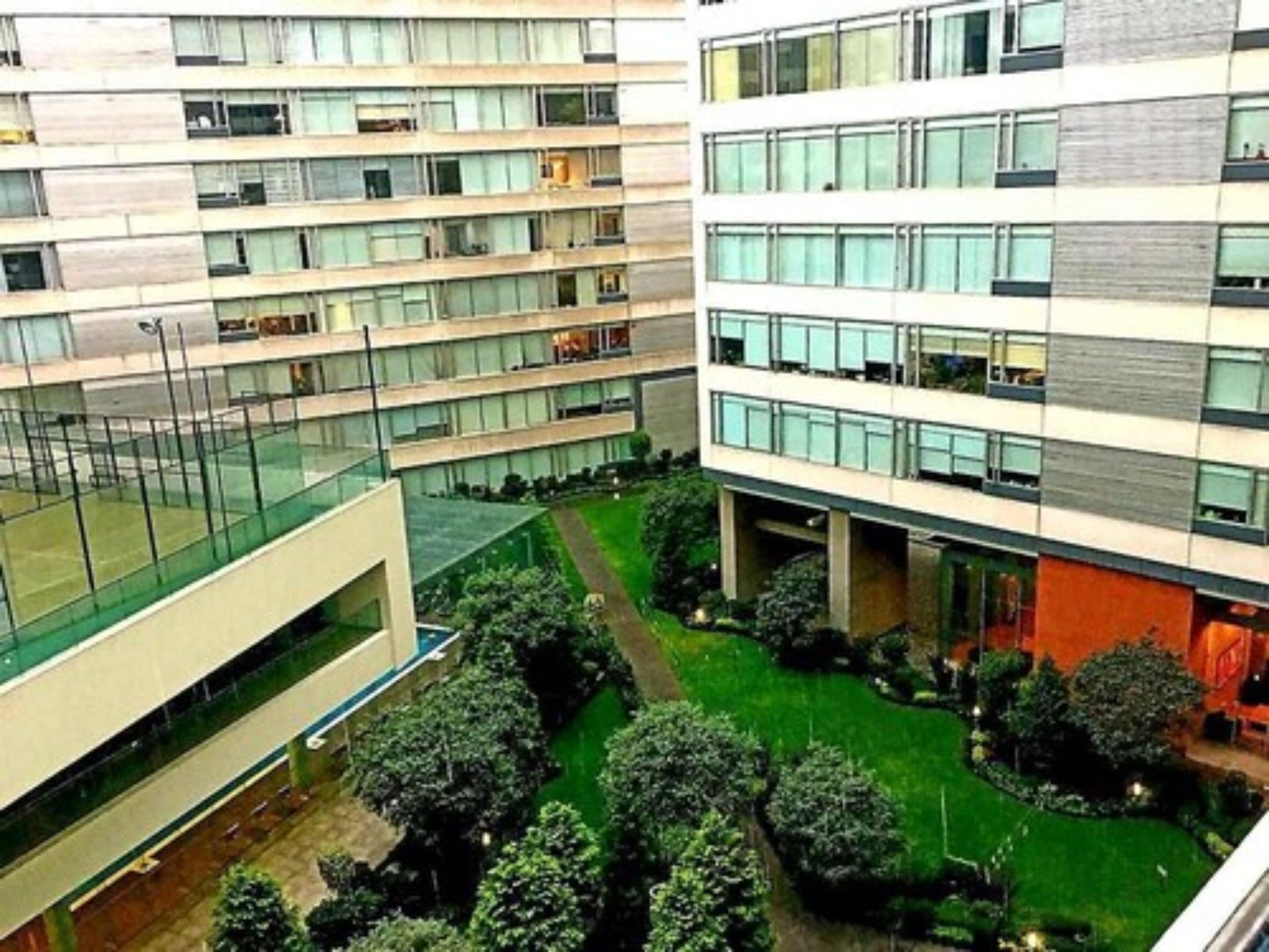 Edifício de vários andares com um pátio central, com gramados verdes e árvores.