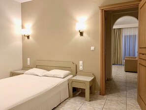 Quarto de hotel com cama, mesas de cabeceira, luminárias fixadas na parede, guarda-roupa de madeira e vista para uma varanda com cortinas.