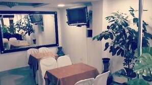 Quarto com um espelho grande, televisão na parede, mesa com cadeiras e um vaso de planta.