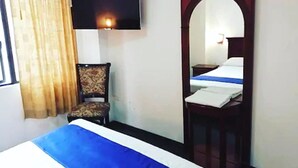 Quarto de hotel com cama, cadeira, televisão fixada na parede e espelho com arco.