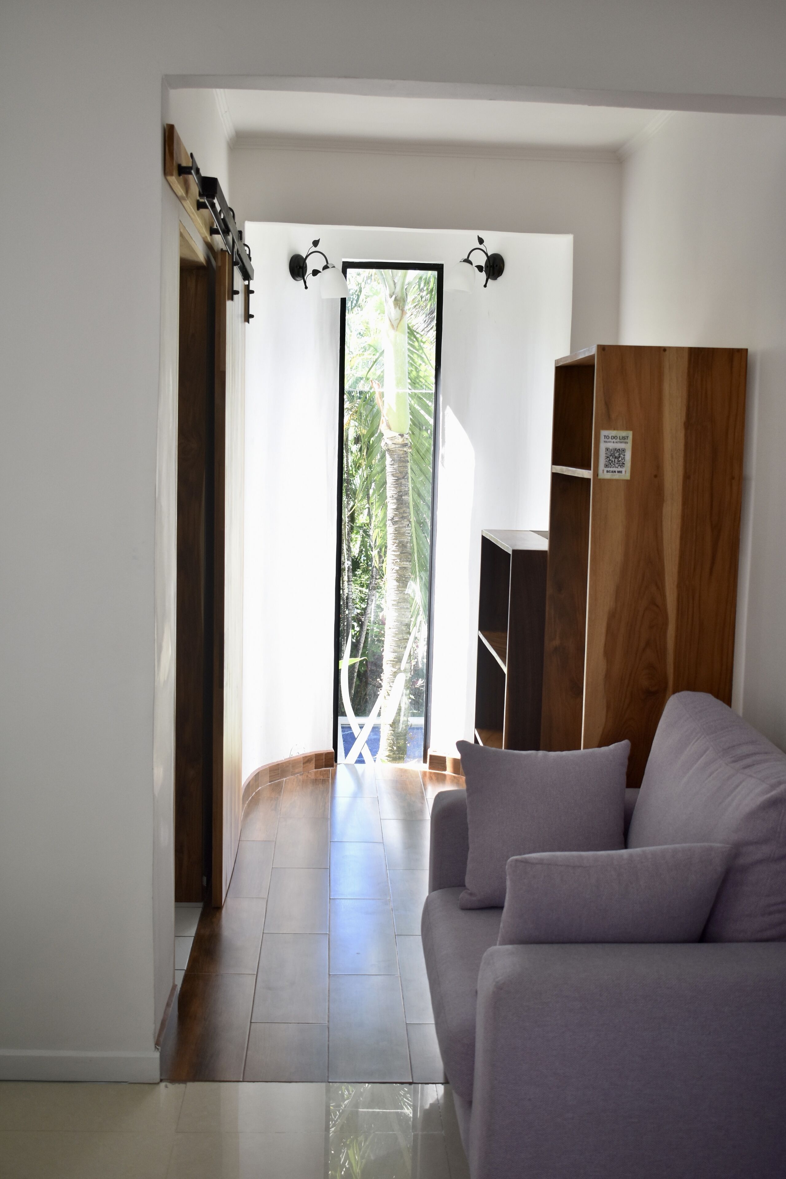 Uma sala de estar moderna com um sofá cinza, um armário de madeira e vista para o verde lá fora.