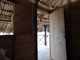 Um quarto de madeira com telhado de palha, uma porta visível e vista para área externa.