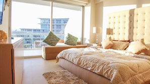Quarto moderno com uma cama grande, um sofá e vista para um edifício através de grandes janelas.