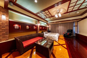 Quarto de hotel com uma cama grande, um sofá, uma poltrona de massagem e uma mesa com tampo de vidro.