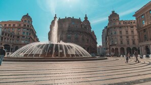Uma fonte em uma praça com arquitetura clássica ao fundo.